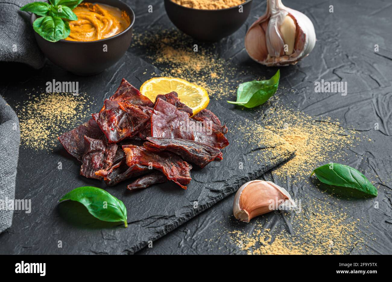 Thin slices of dried meat on a glossy black background with spices ...