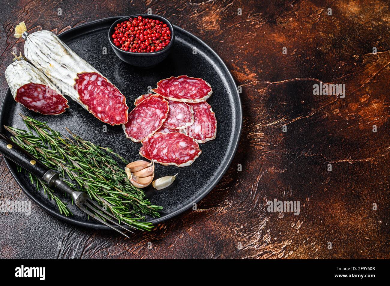 Italian sliced salami on a plate with rosemary and thyme. Dark ...