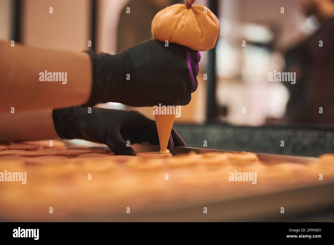 Skilled pastry chef using syringe with icing while making macarons ...