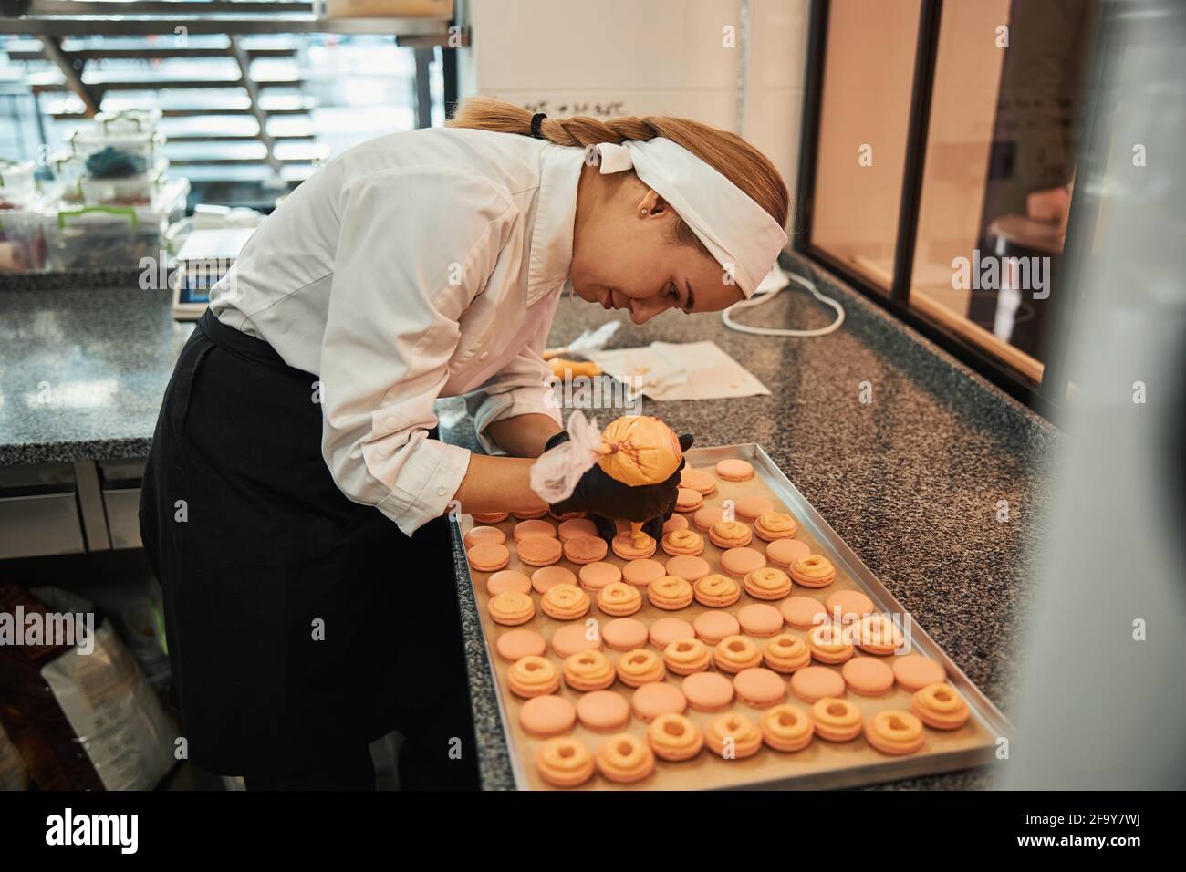 Focused pastry chef putting icing on custom-made macarons Stock Photo ...