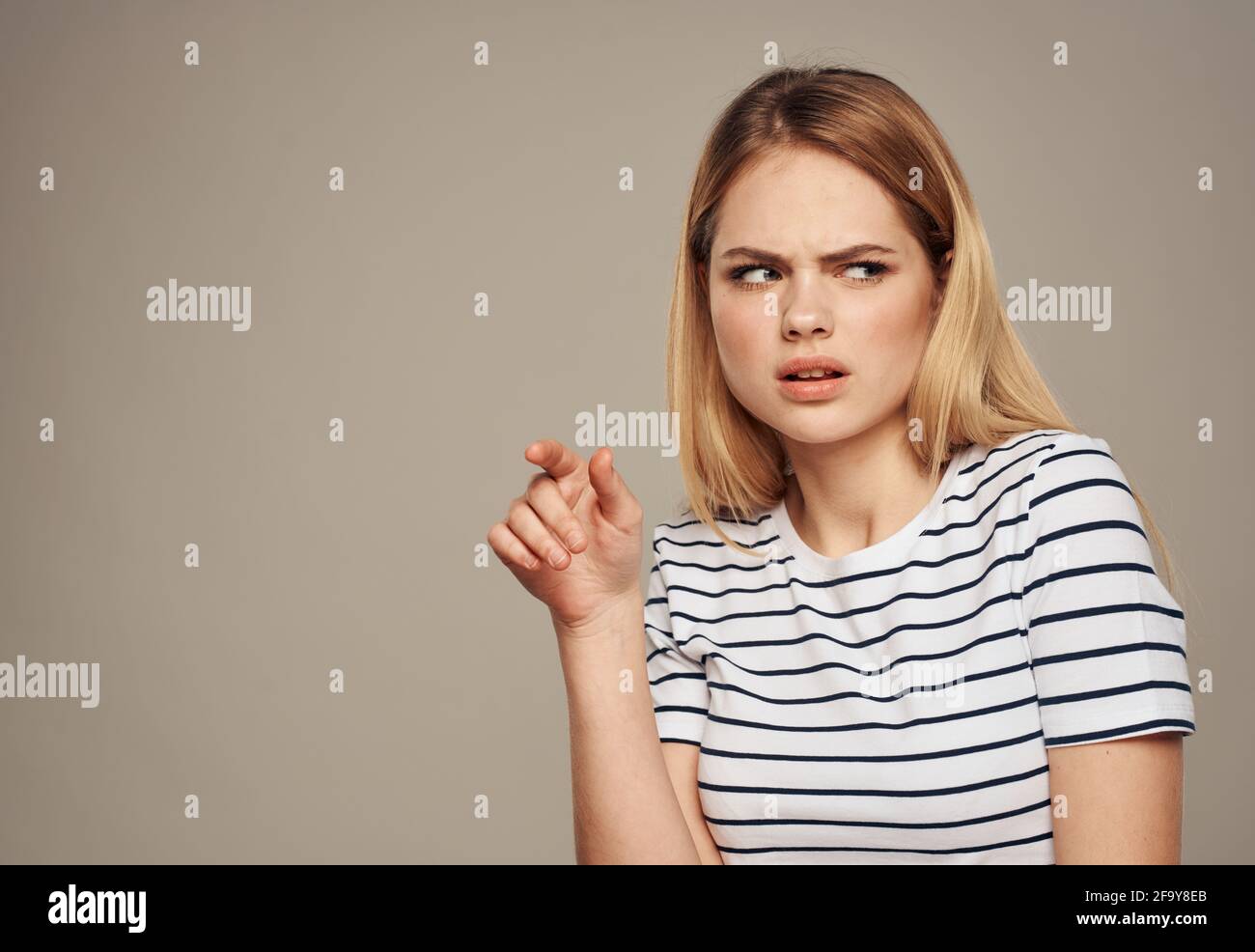 Blond woman with disgust looks to the side and beige background cropped ...