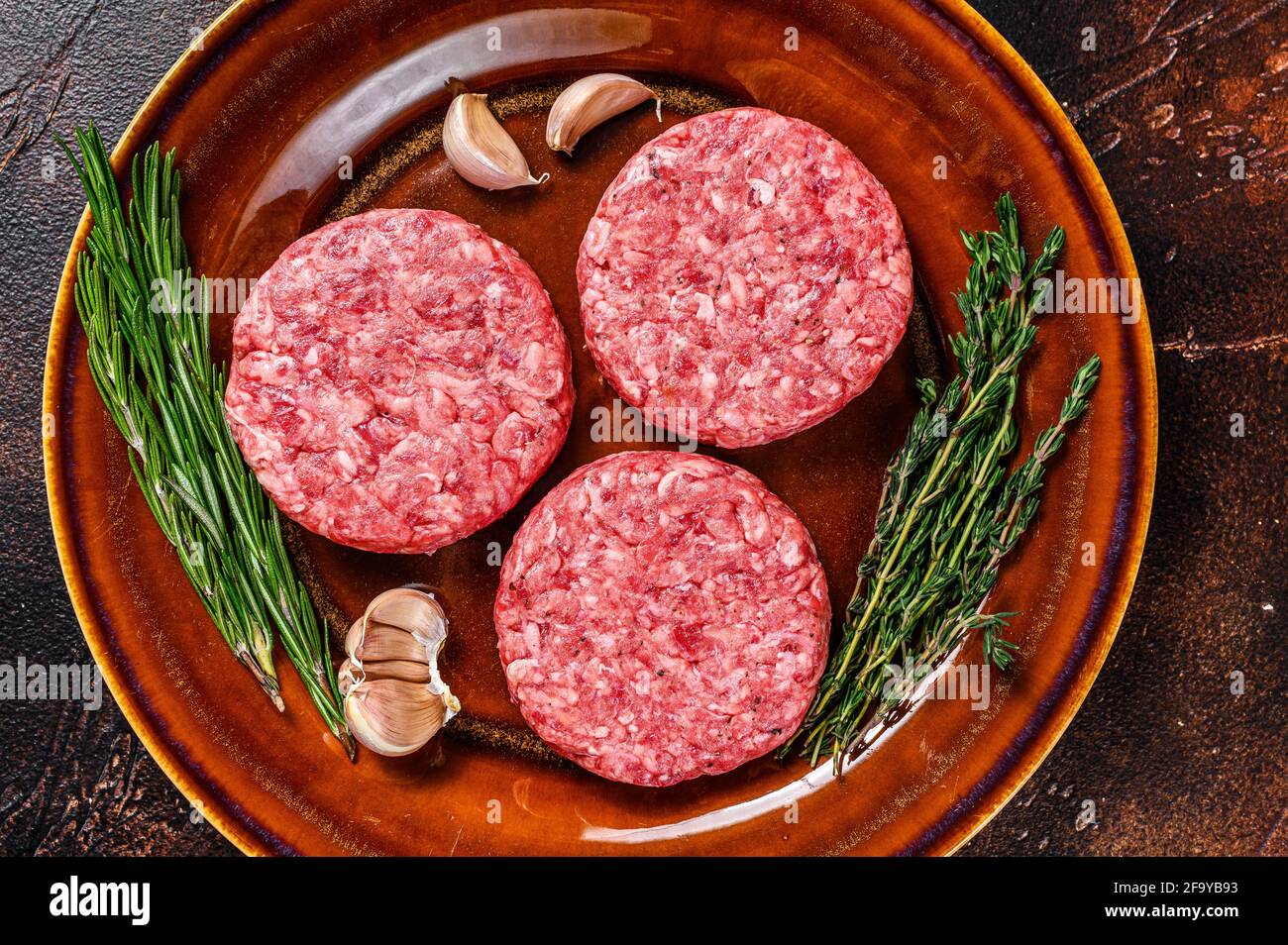 Raw burger meat cutlets with mince beef and herbs on a plate. Dark ...