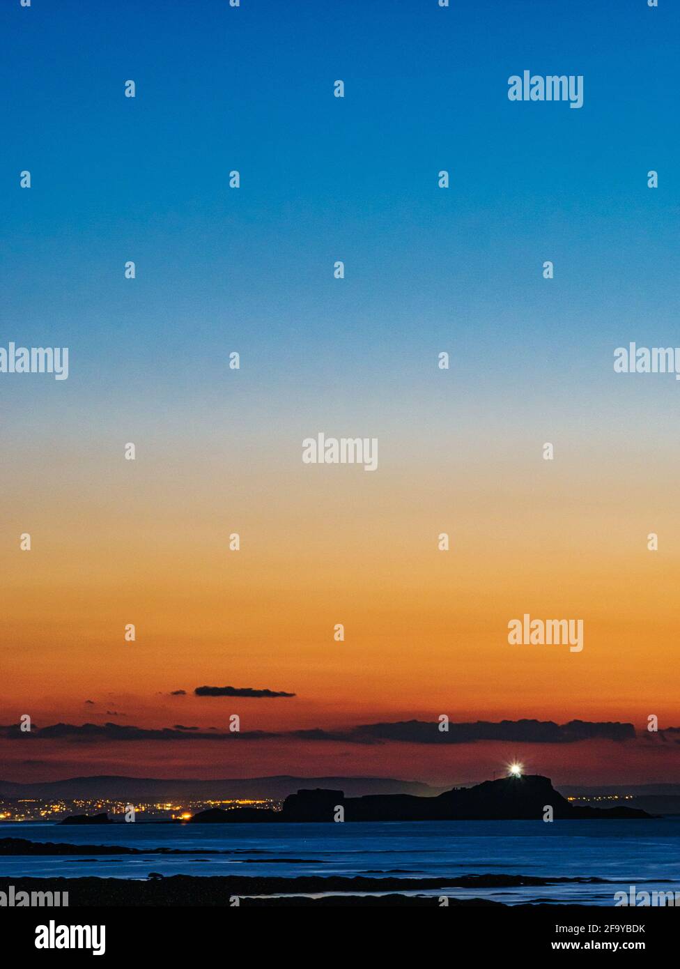 Silhouette of Fidra Island with light from the lighthouse at sunset ...