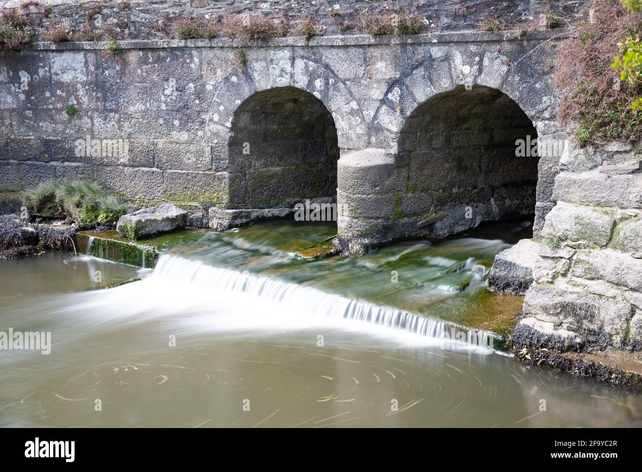 The Helford River flows under an old stone bridge in Gweek, Cornwall ...