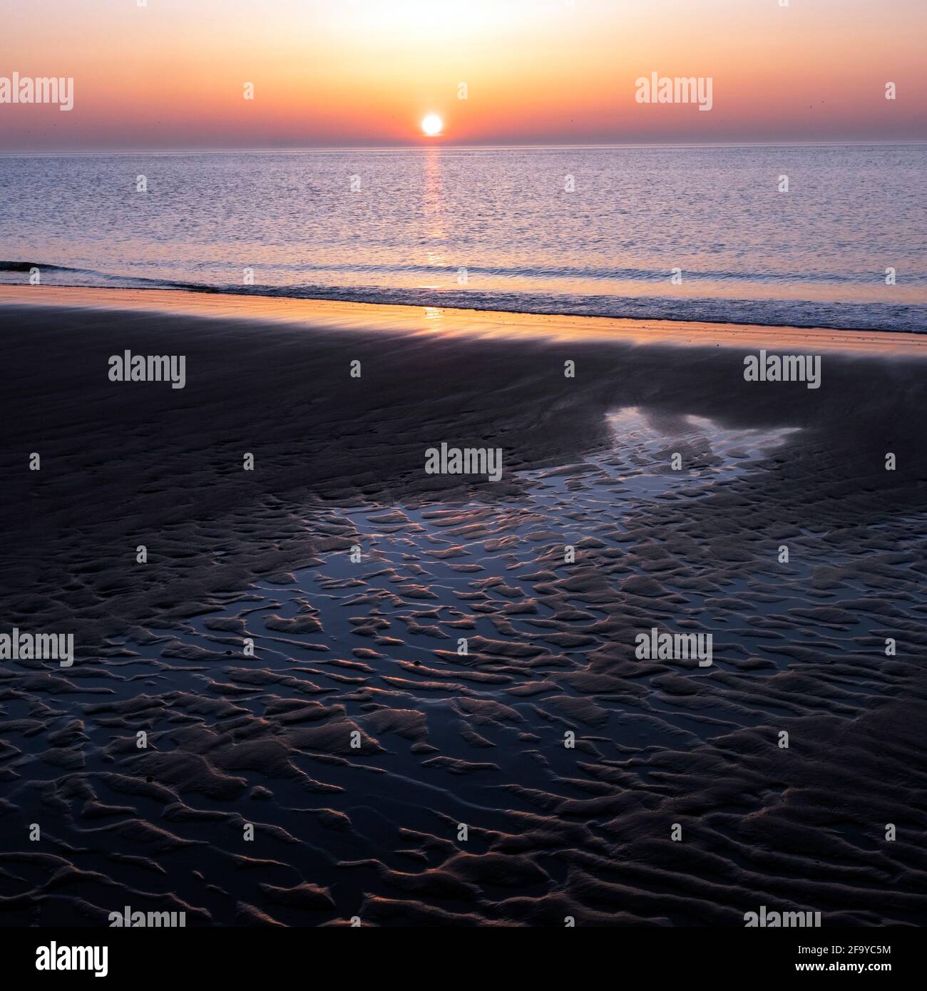 pattern in sand and colorful reflection of setting sun in water Stock ...