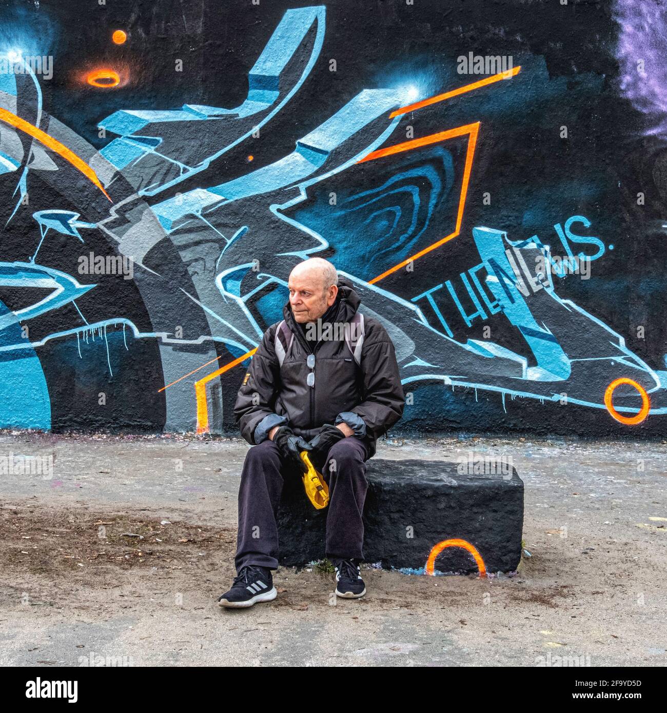 Senior elderly man sitting on bench next to artwork on wall in ...
