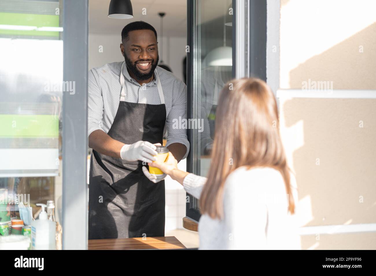 A cheerful and smiling African-American waiter is serving female ...