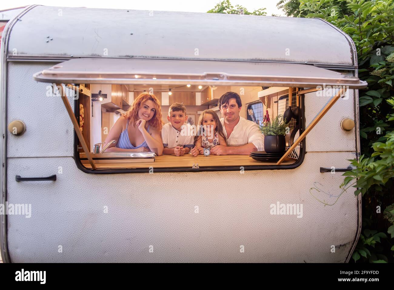 Cheerful family of travelers look out from mobile home, trailer house ...