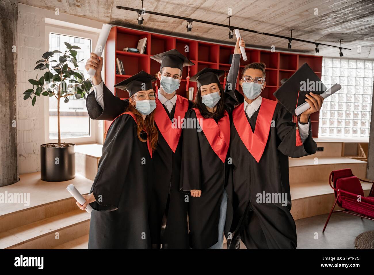 multiethnic students in medical masks, gowns and caps holding diploma ...