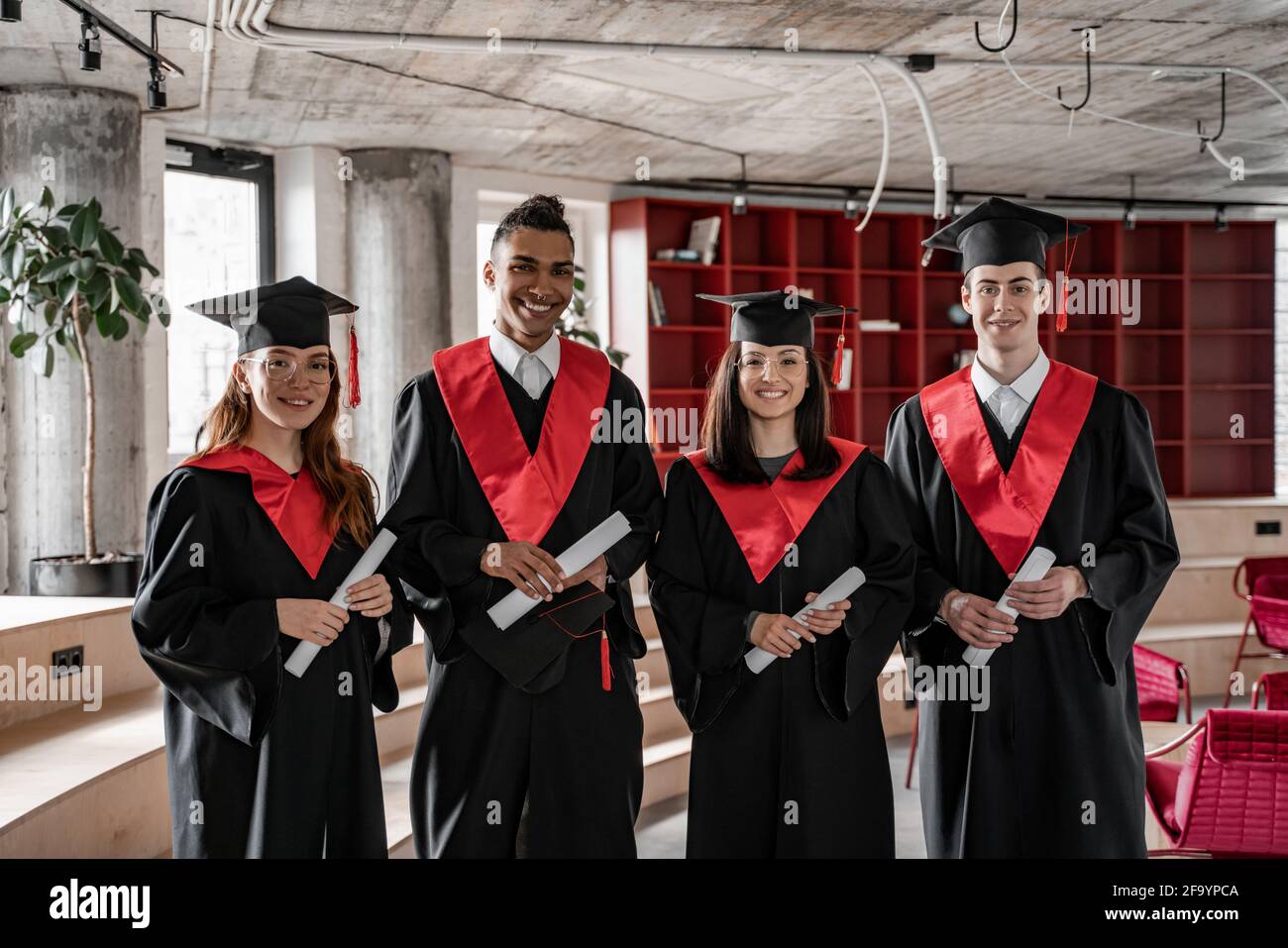 happy interracial students in graduation gowns and caps holding diploma ...
