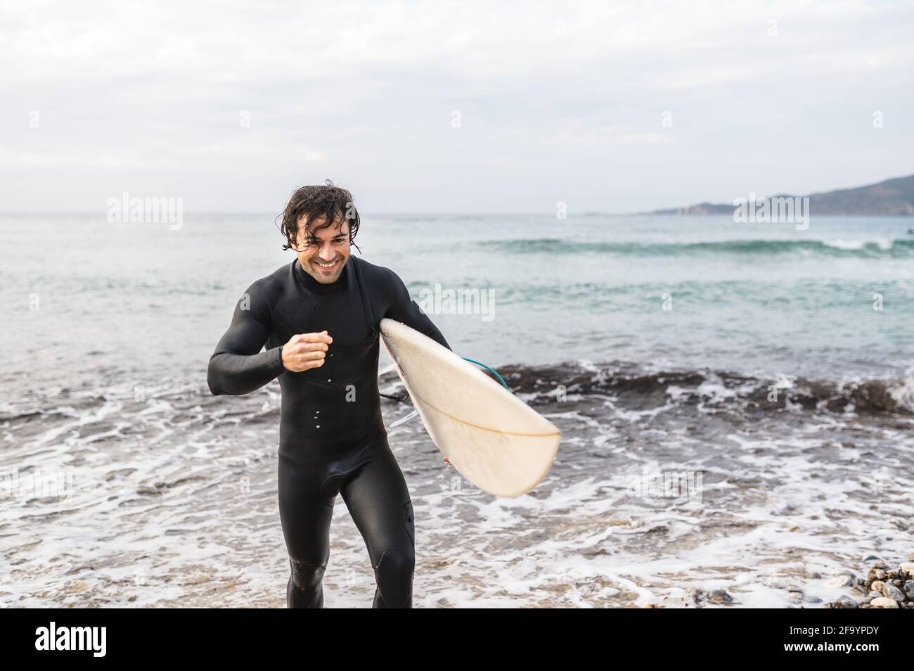Happy surfer getting out of the water after surfing with smiling face ...