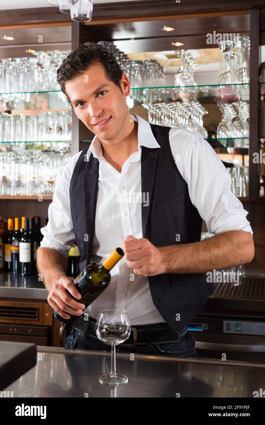 Barman standing behind the bar In restaurant opening a wine bottle ...
