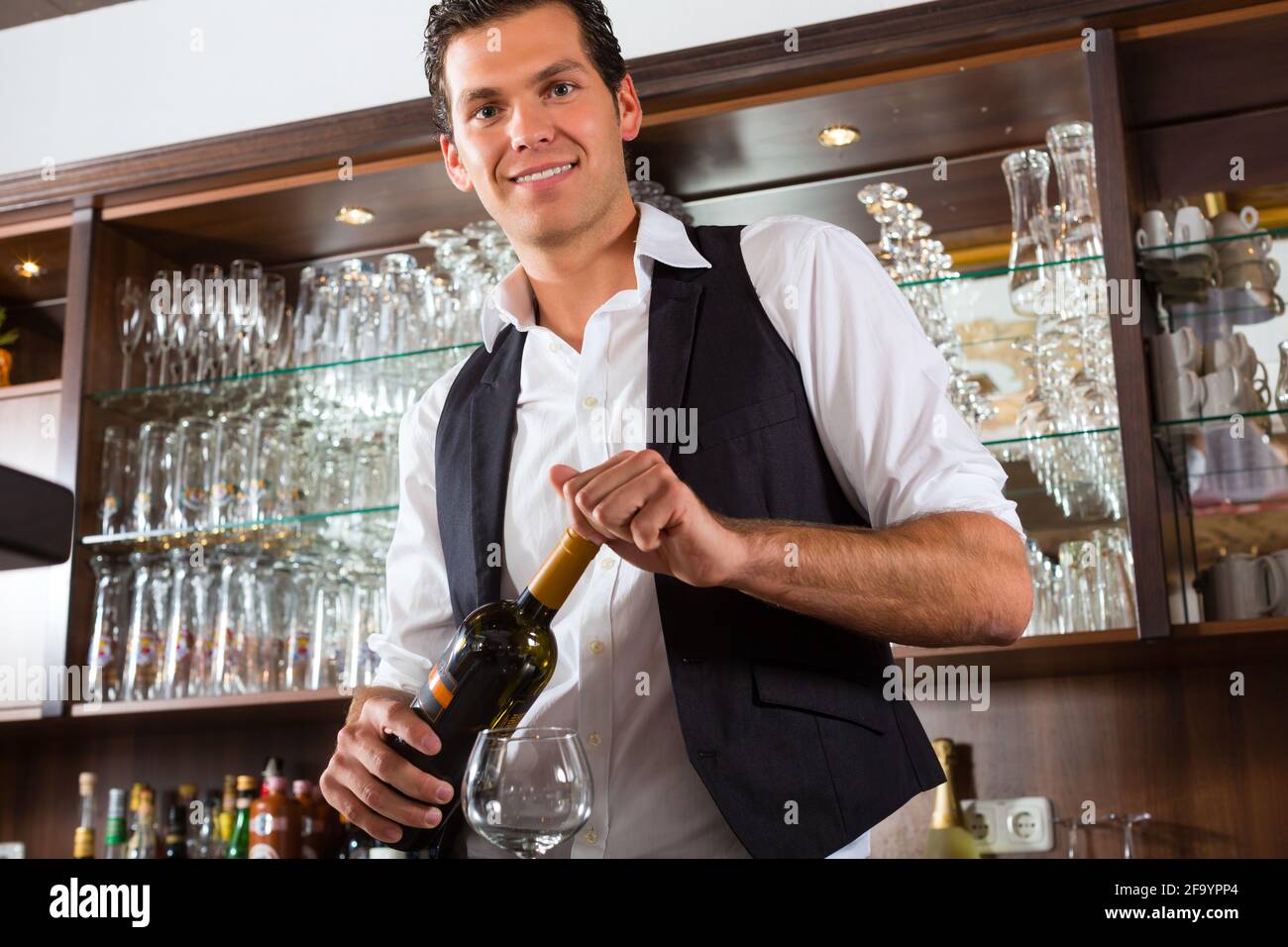 Barman standing behind the bar In restaurant opening a wine bottle ...