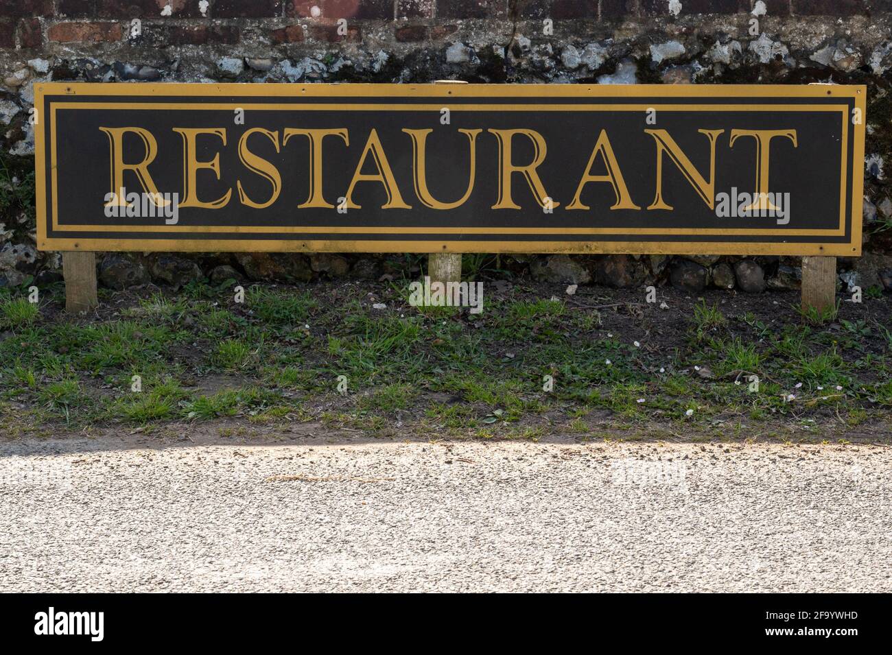 An oblong black and gold coloured Restaurant sign against a stone wall ...