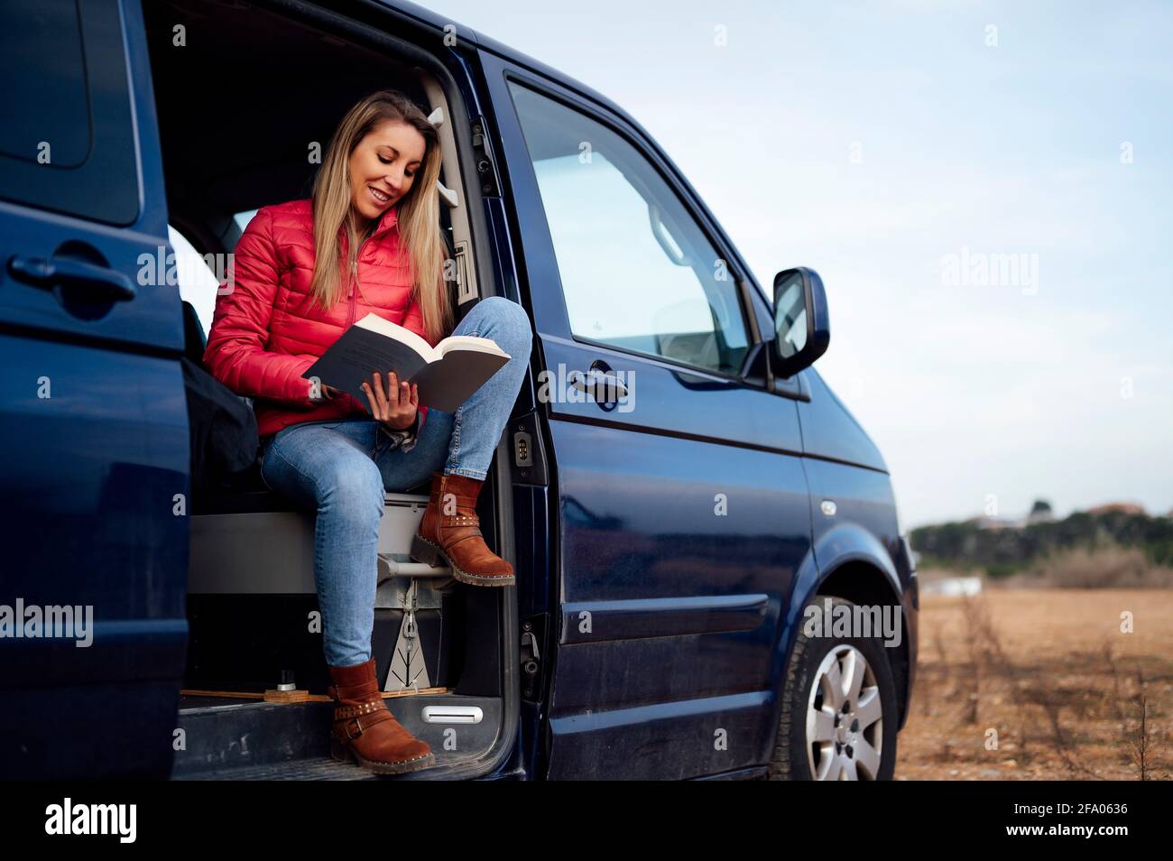 Happy woman reading book on door of camper van Stock Photo - Alamy
