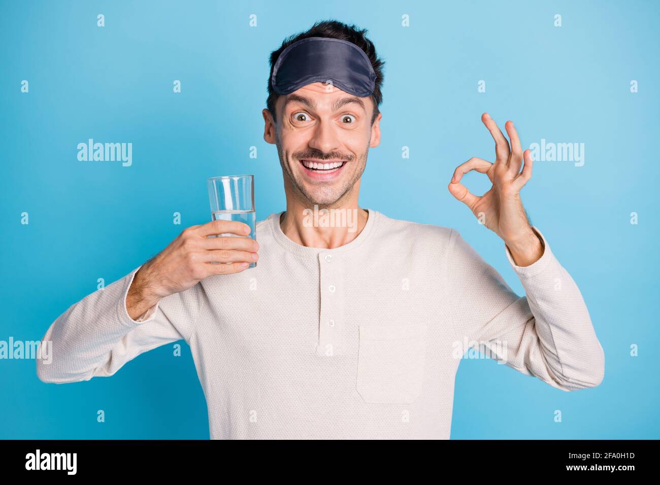 Photo portrait of excited man holding glass of water in one hand showing ok sign isolated on ...