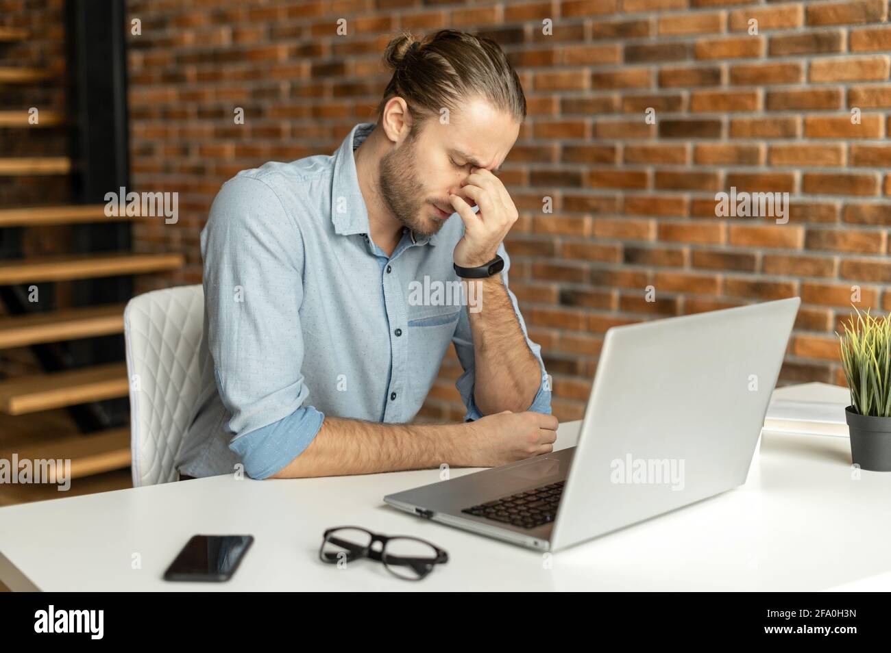 Fatigued hipster using laptop for working, a guy in smart casual wear ...