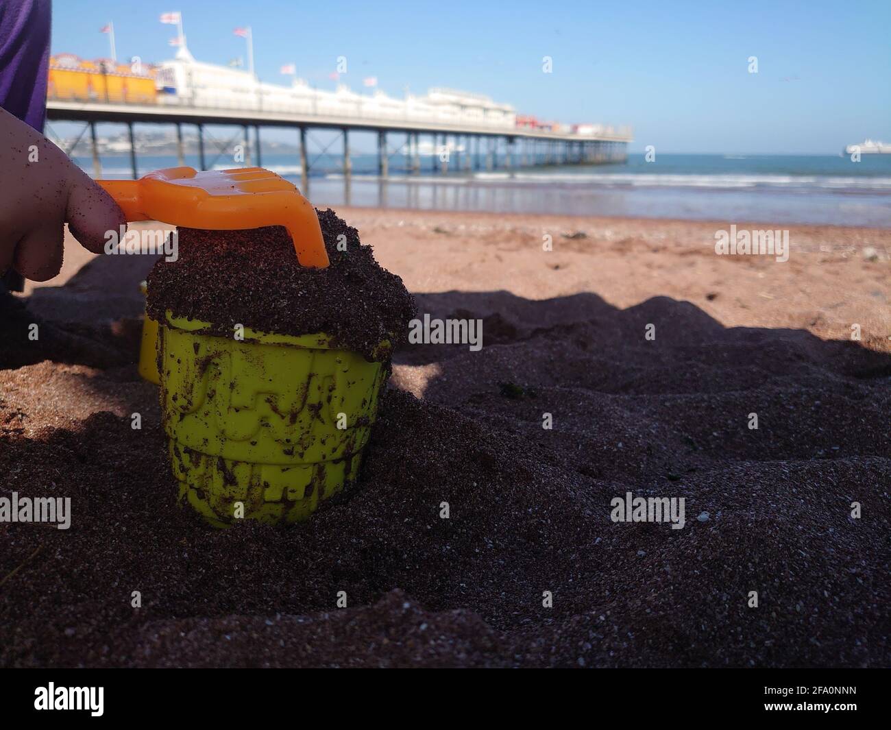 Child is playing on the sandy beach with a plastic bucket and shovel ...