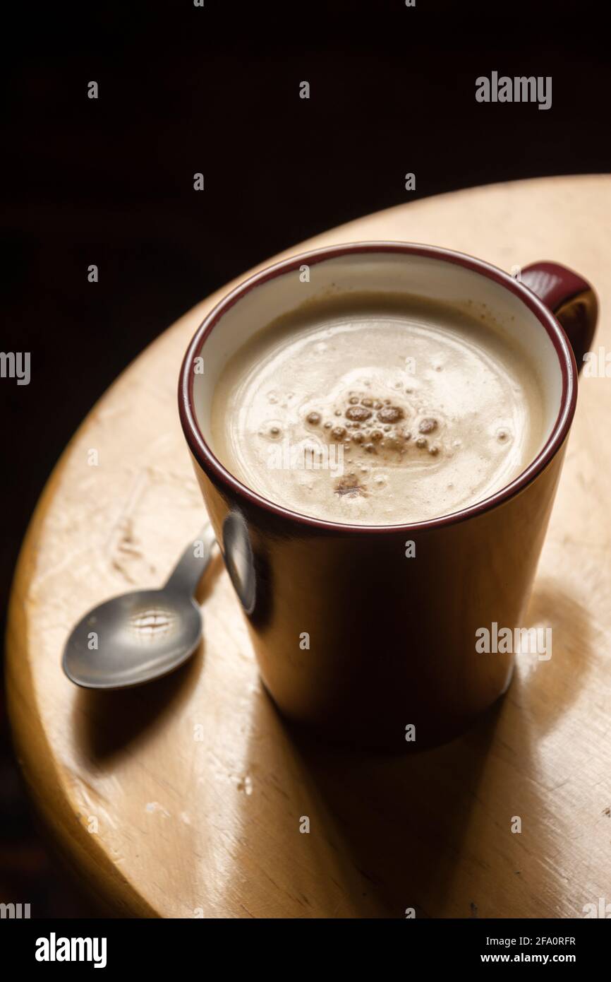 Aerial view of cup of cappuccino coffee and spoon on wooden stool, on ...