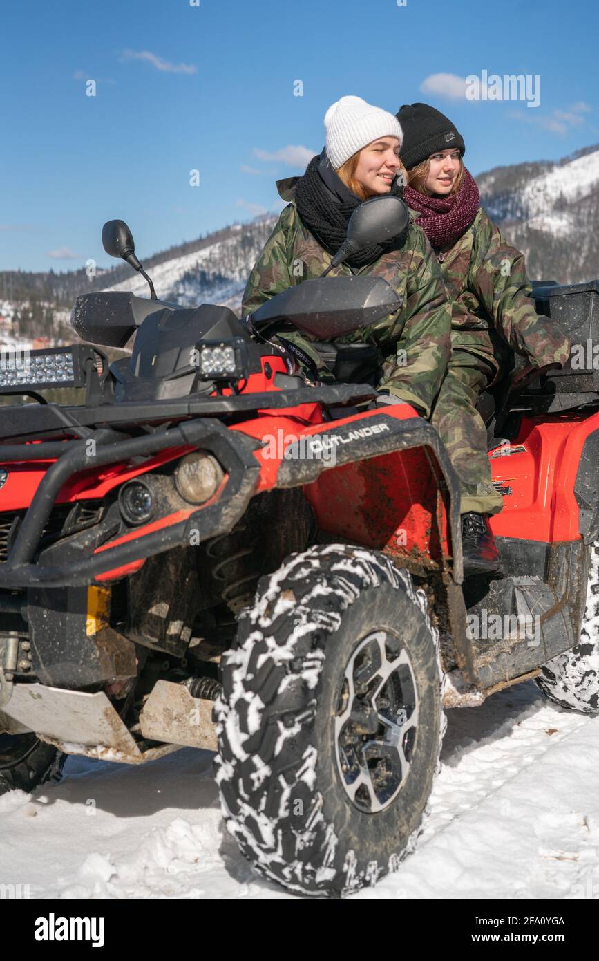 A group of young people ride ATVs in the snow-capped mountains ...