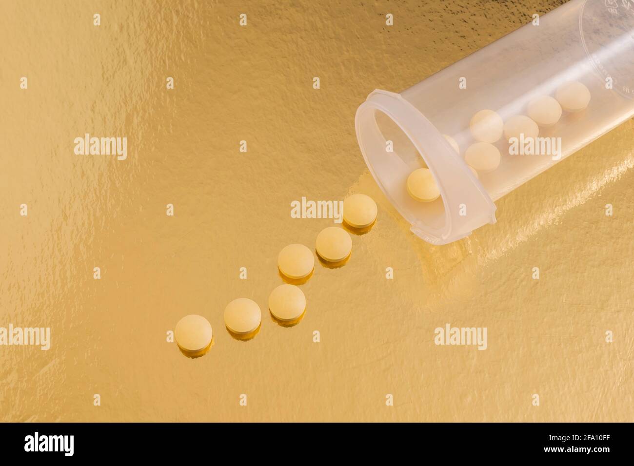 Yellow medicinal pills and translucent plastic bottle on shiny gold ...