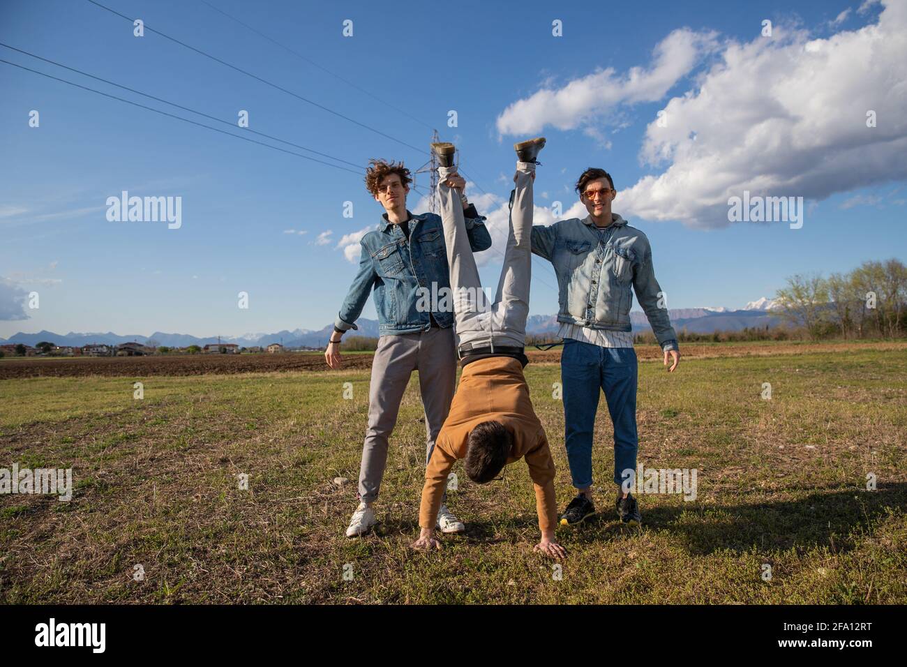 A group of friends play in a meadow, two friends lift a friend by his ...