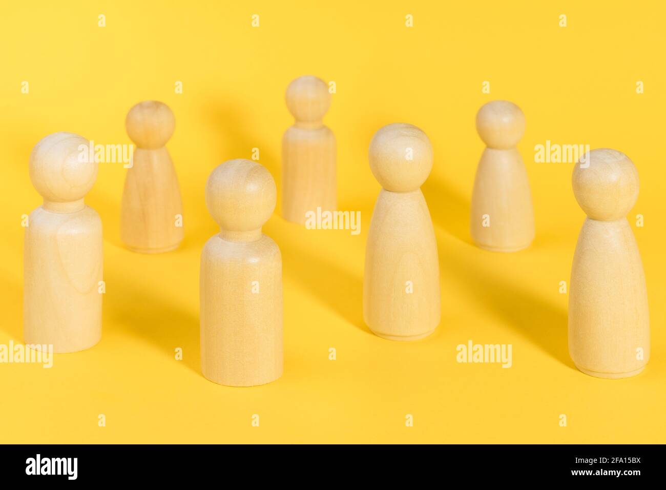 Wooden people figures stand on yellow backdrop, relationship ...