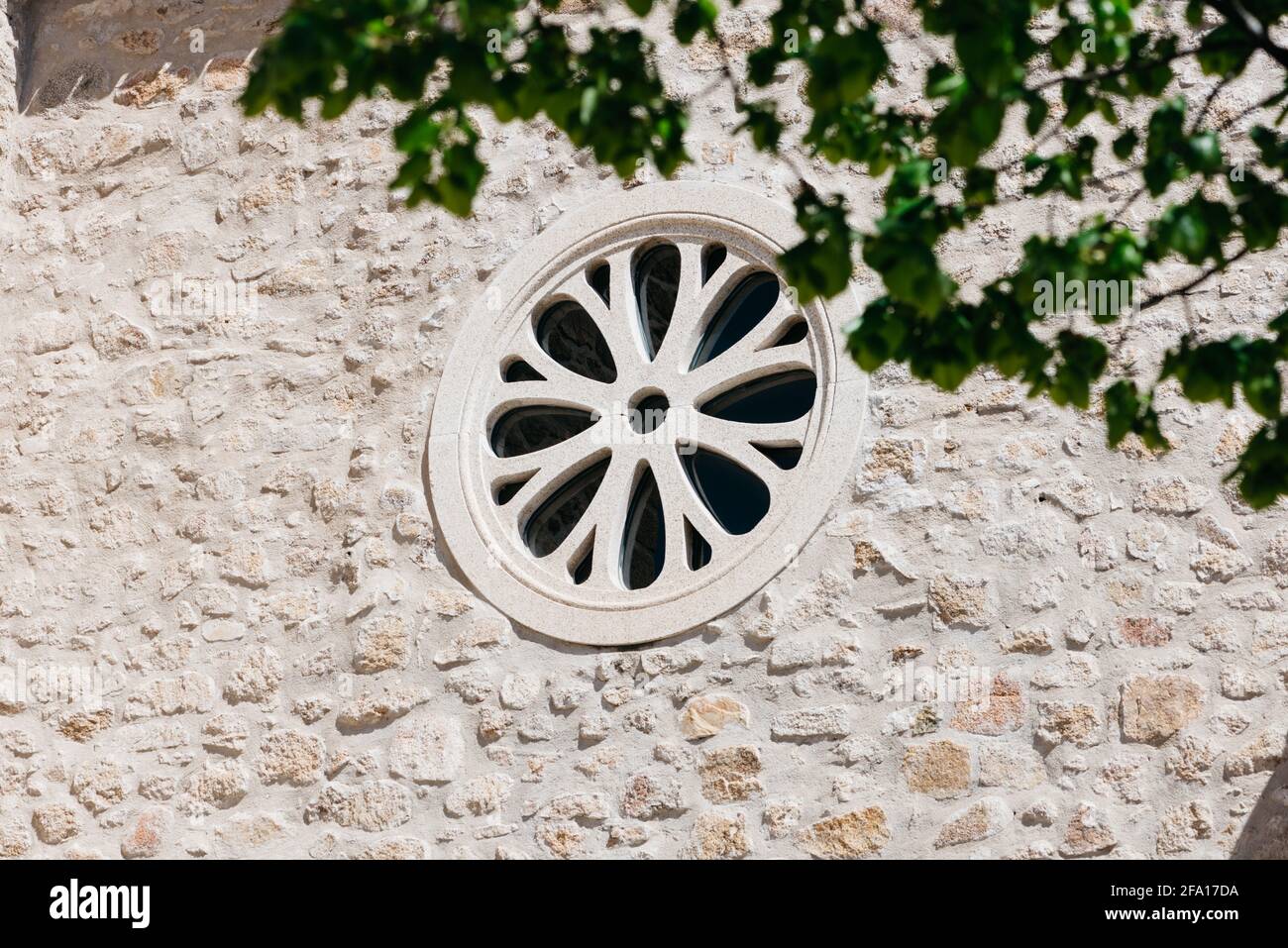 Round window texture of a church on the stone wall with a tree branch ...