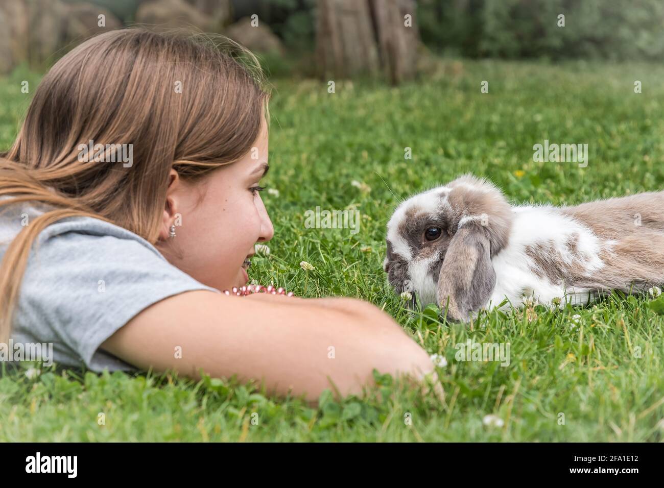 Teenager girl and her rabbit lying in the green grass, looking at each ...
