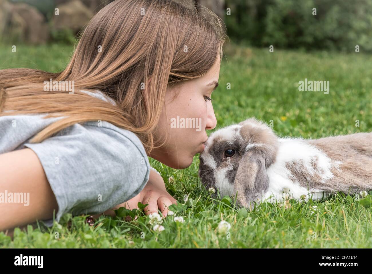 Teenager kissing her rabbit, both lying in the green grass Stock Photo ...