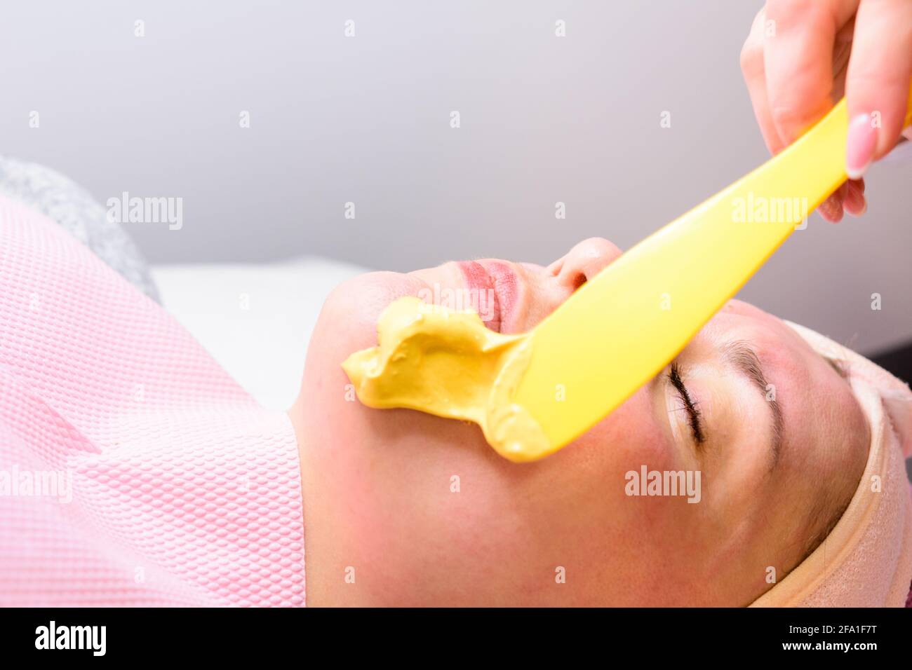 Applying a golden mask on the face after the cleansing procedure, an ...