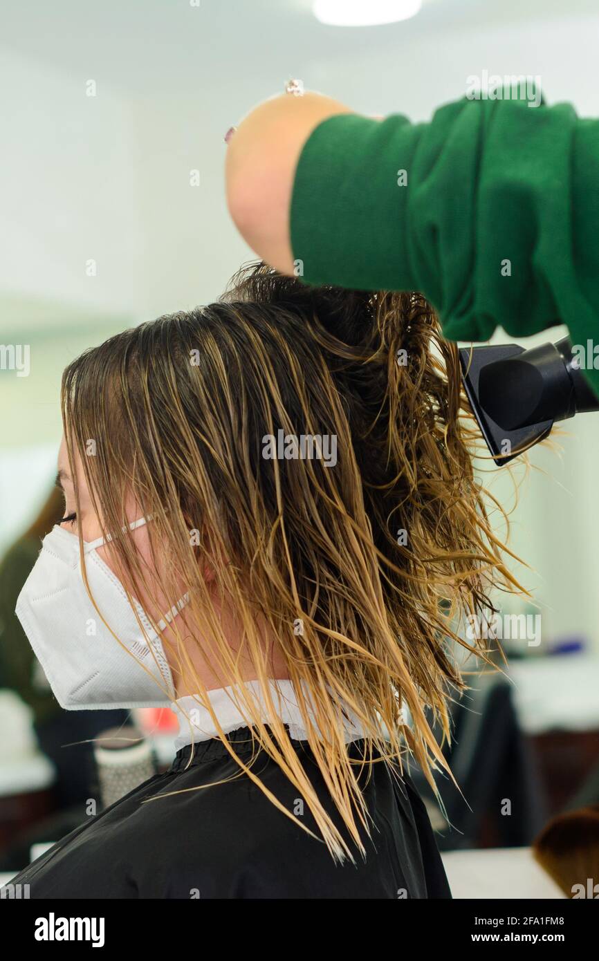 Hairdresser in a mask with at work, drying hair in a barbershop, client ...