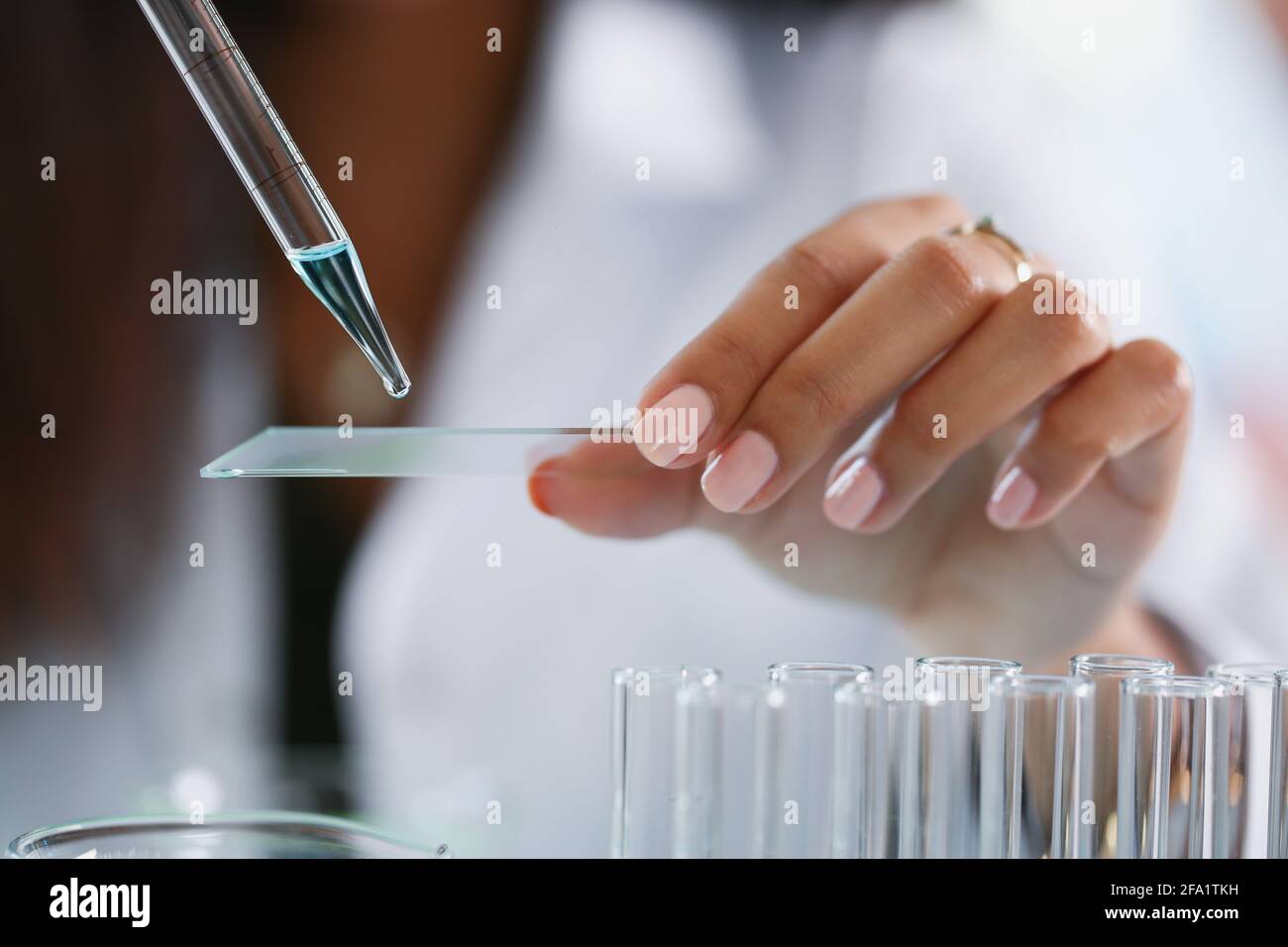 Scientist dripping blue liquid from pipette onto glass slide closeup ...