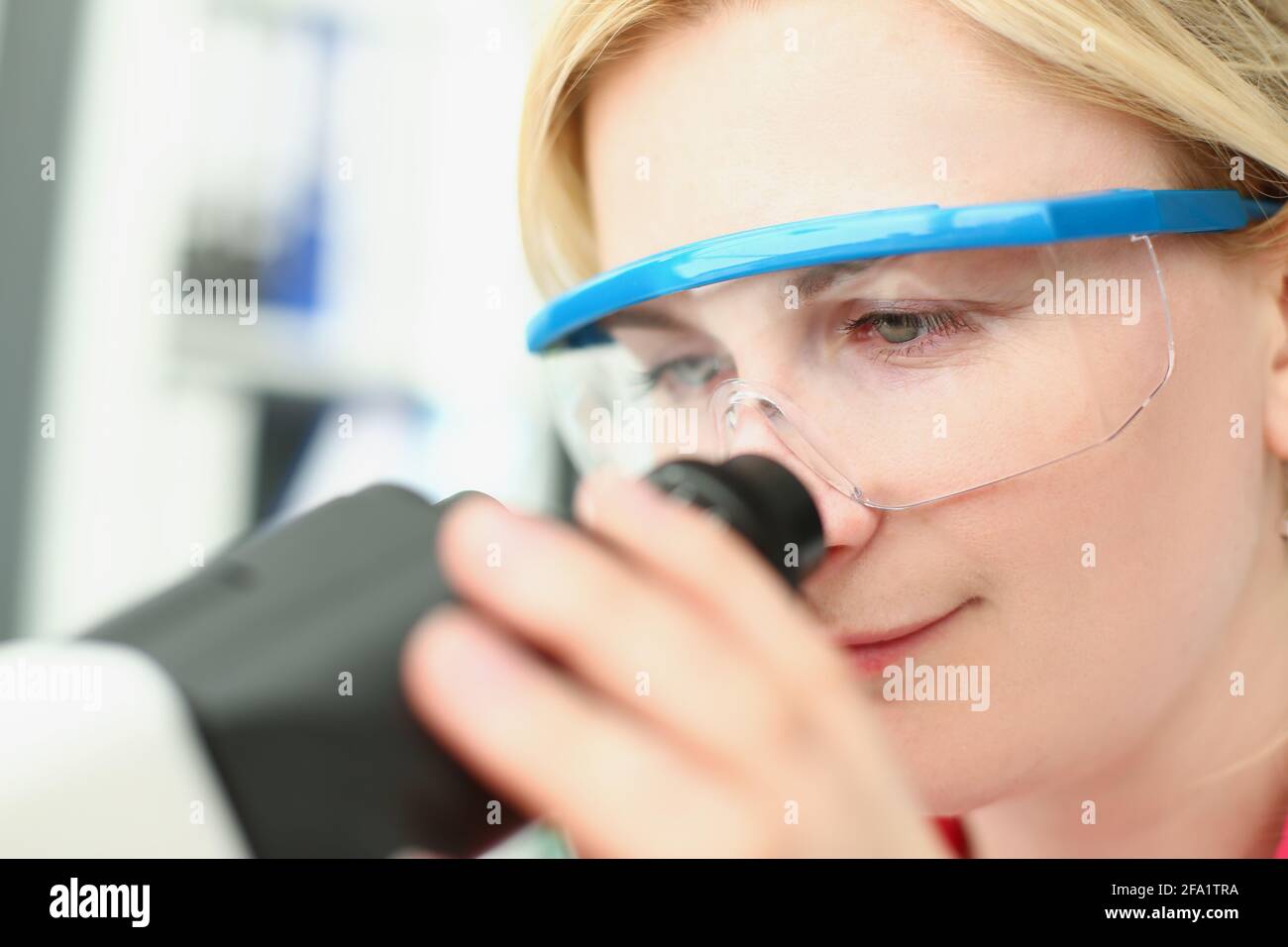 Woman chemist in safety glasses looking through microscope Stock Photo ...