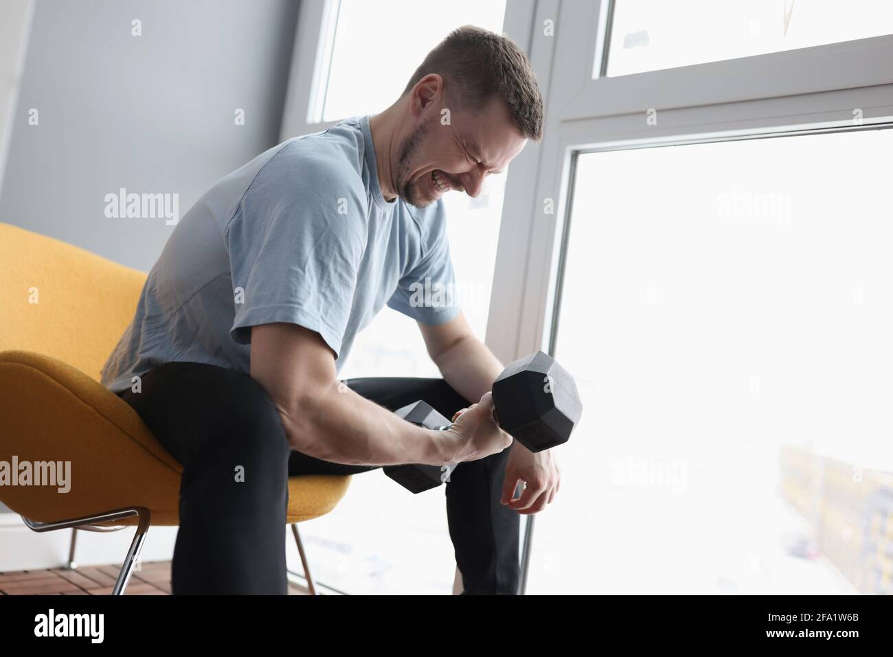 Young man sitting on chair and lifting heavy dumbbell Stock Photo - Alamy