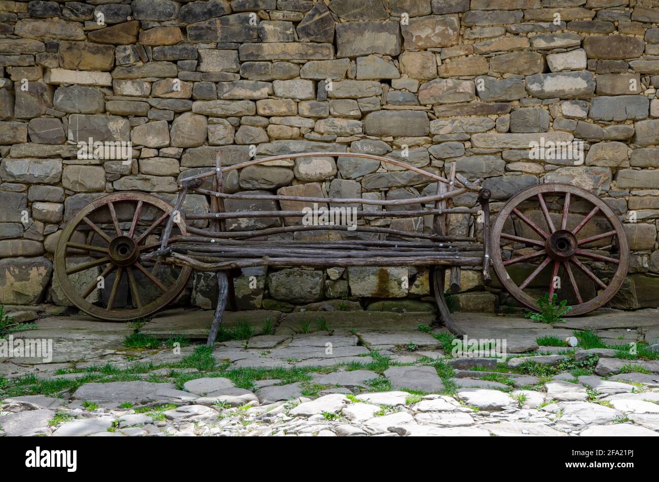 Empty wooden bench stands near stone wall with two wagon wheels aside ...
