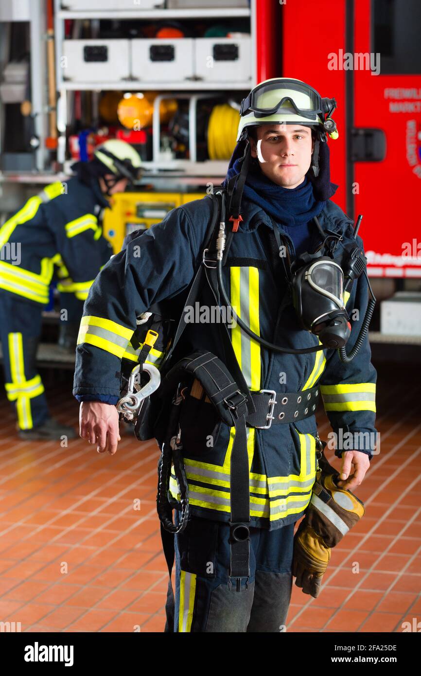 young fireman in uniform standing in front of firetruck, he is ready ...