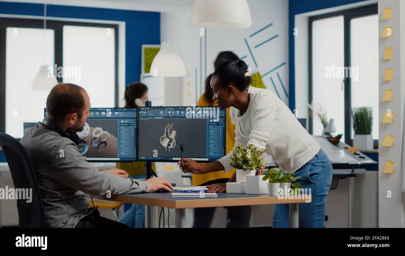 Diverse team of engineers working on computer at mechanical piece ...