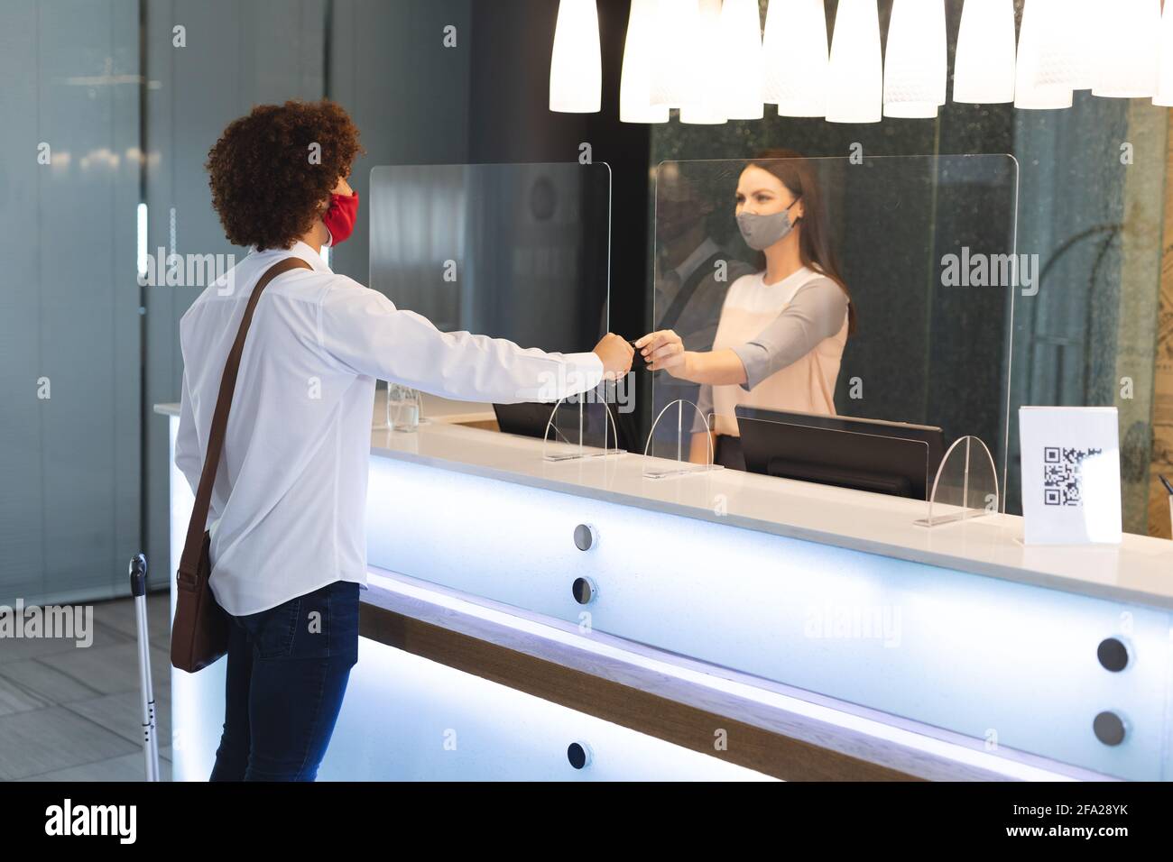 Diverse businessman wearing face mask talking with receptionist in ...
