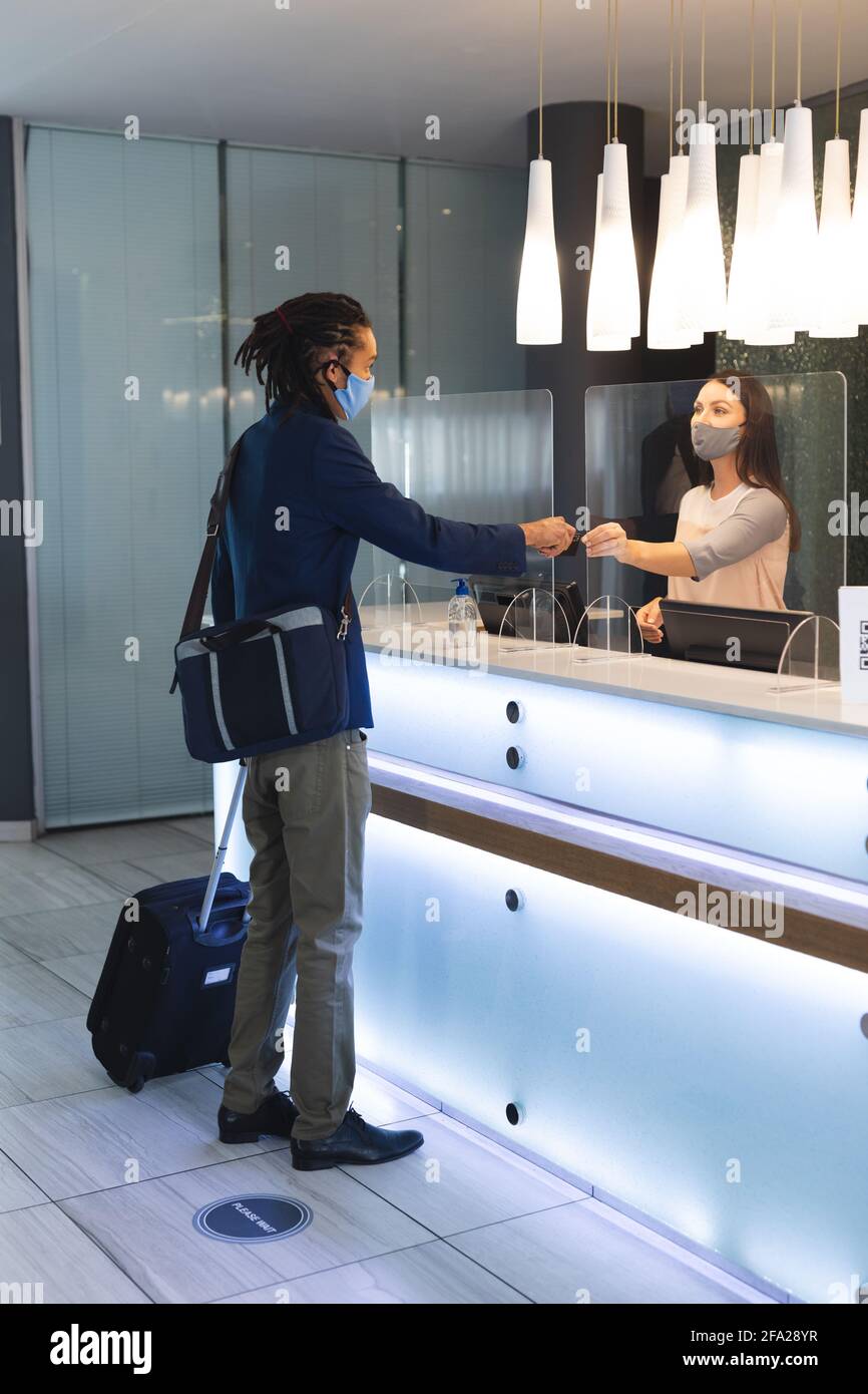 Diverse businessman wearing face mask talking with receptionist in ...