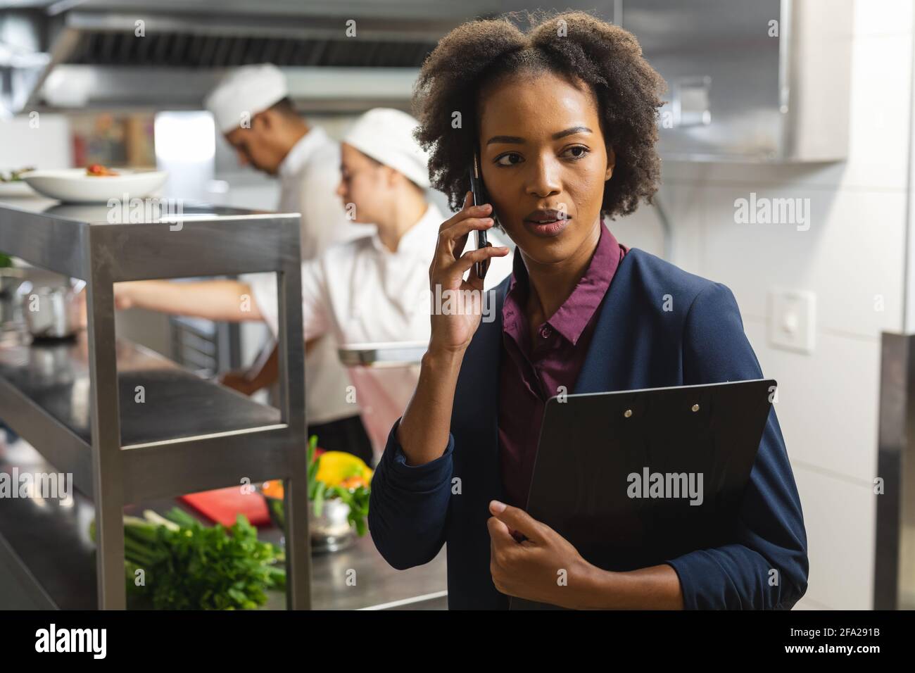 Mixed race kitchen manager talking on the phone with professional chefs ...