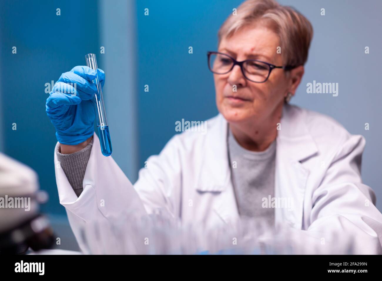 Scientist senior woman looking into test tube for biochemistry test ...