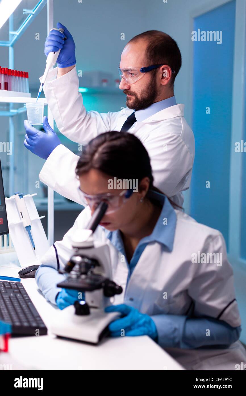 Scientist taking sample with micropipette from test tube and asistant ...