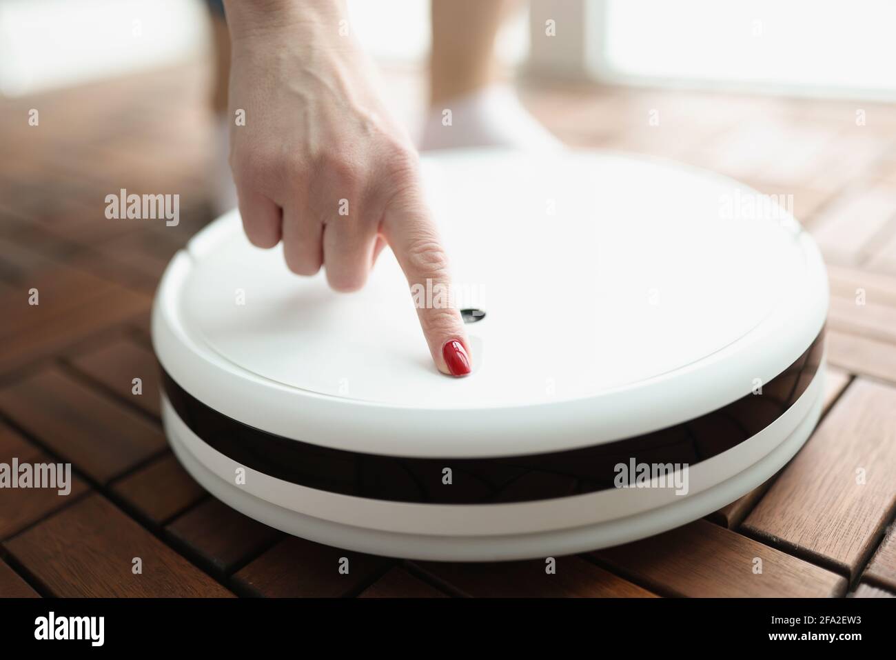 Female finger presses power button on white robotic vacuum cleaner ...