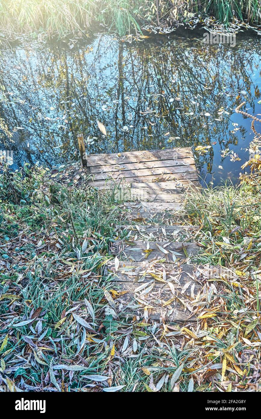 Rustic wooden steps to calm narrow river with green grass covered with ...