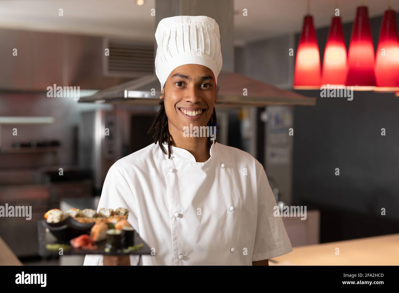Portrait of mixed race professional chef wearing chefs hat serving ...