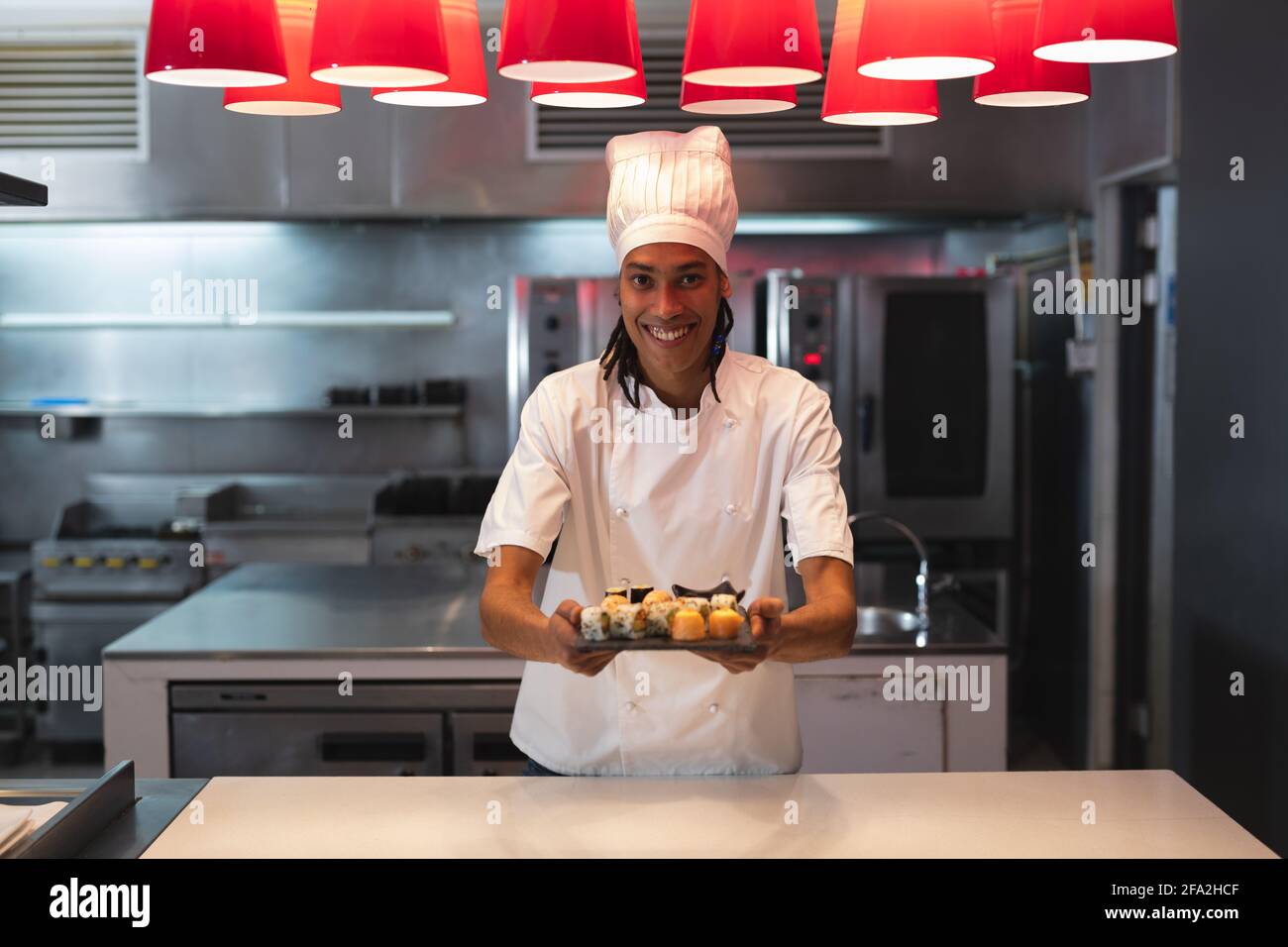 Portrait of mixed race professional chef wearing chefs hat serving ...