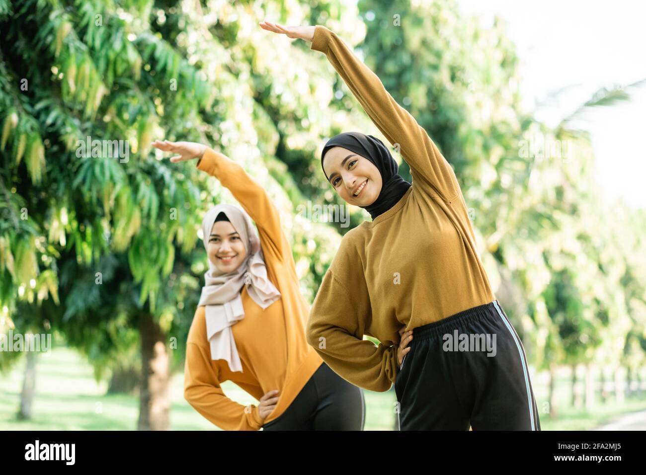two asian girls in veil do arm stretches by raising their arms upward ...