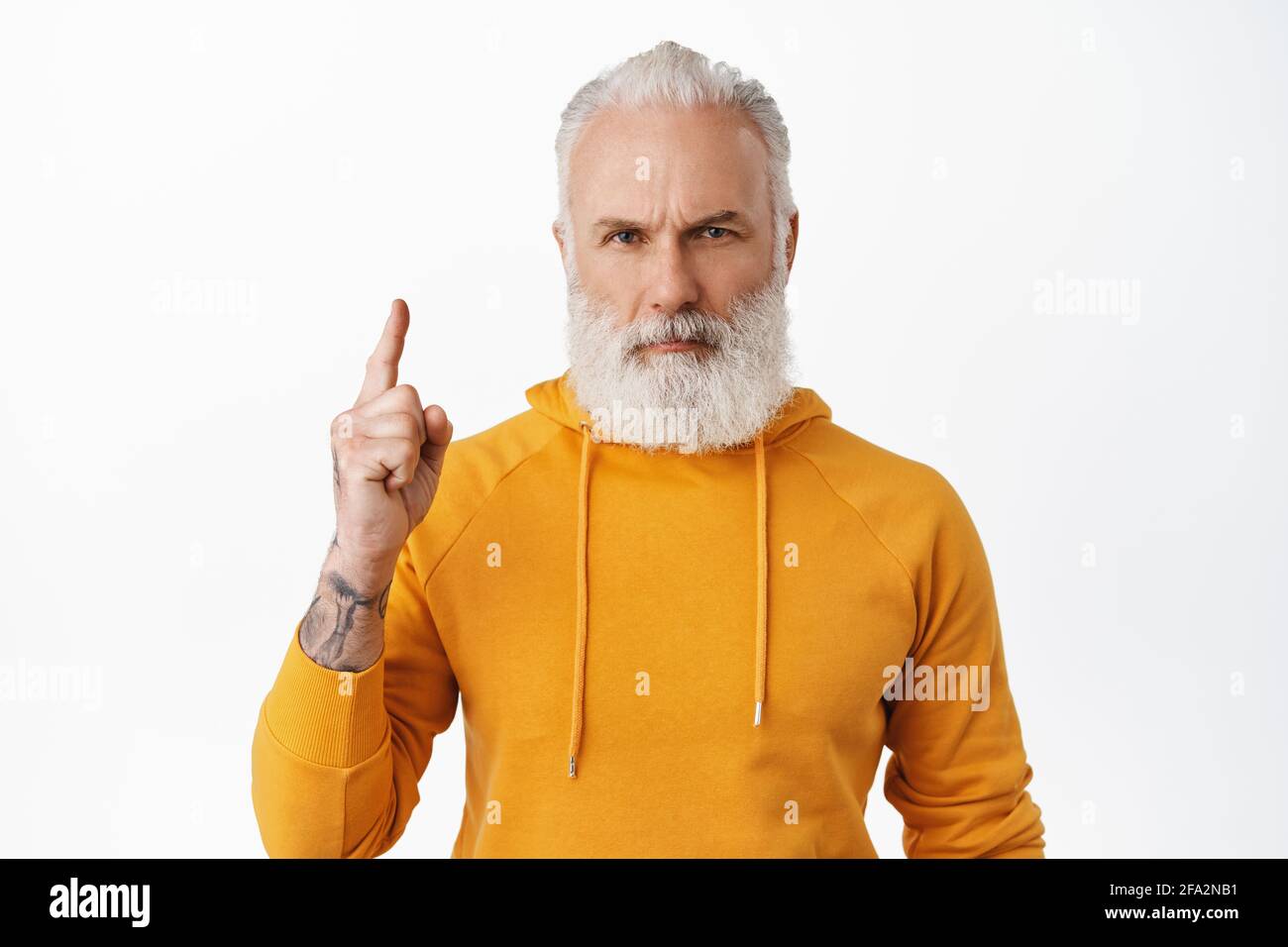 Serious hipster old man frowning, pointing finger up at something ...