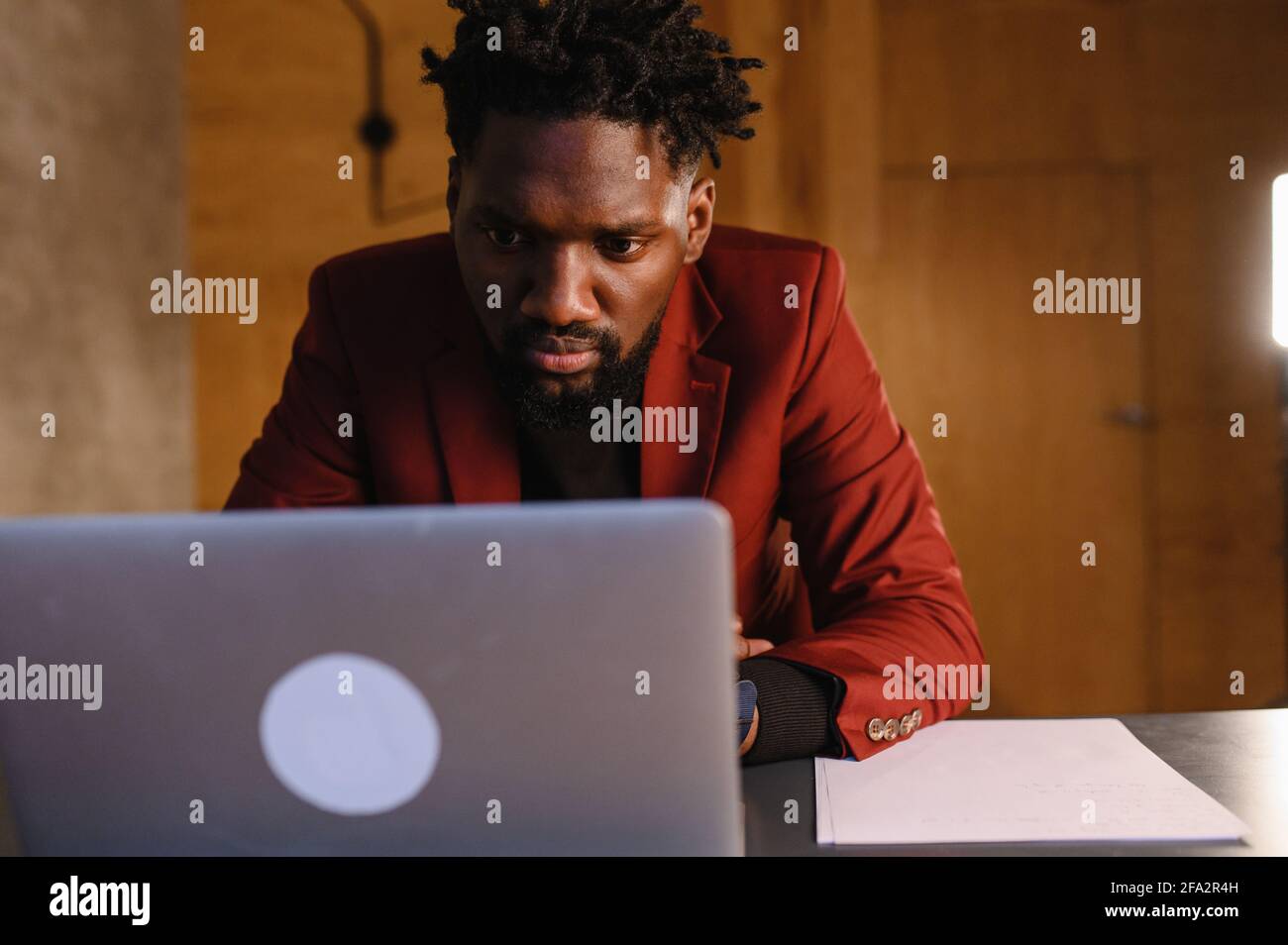 a focused black man in a suit is working on a laptop. Remote work from ...